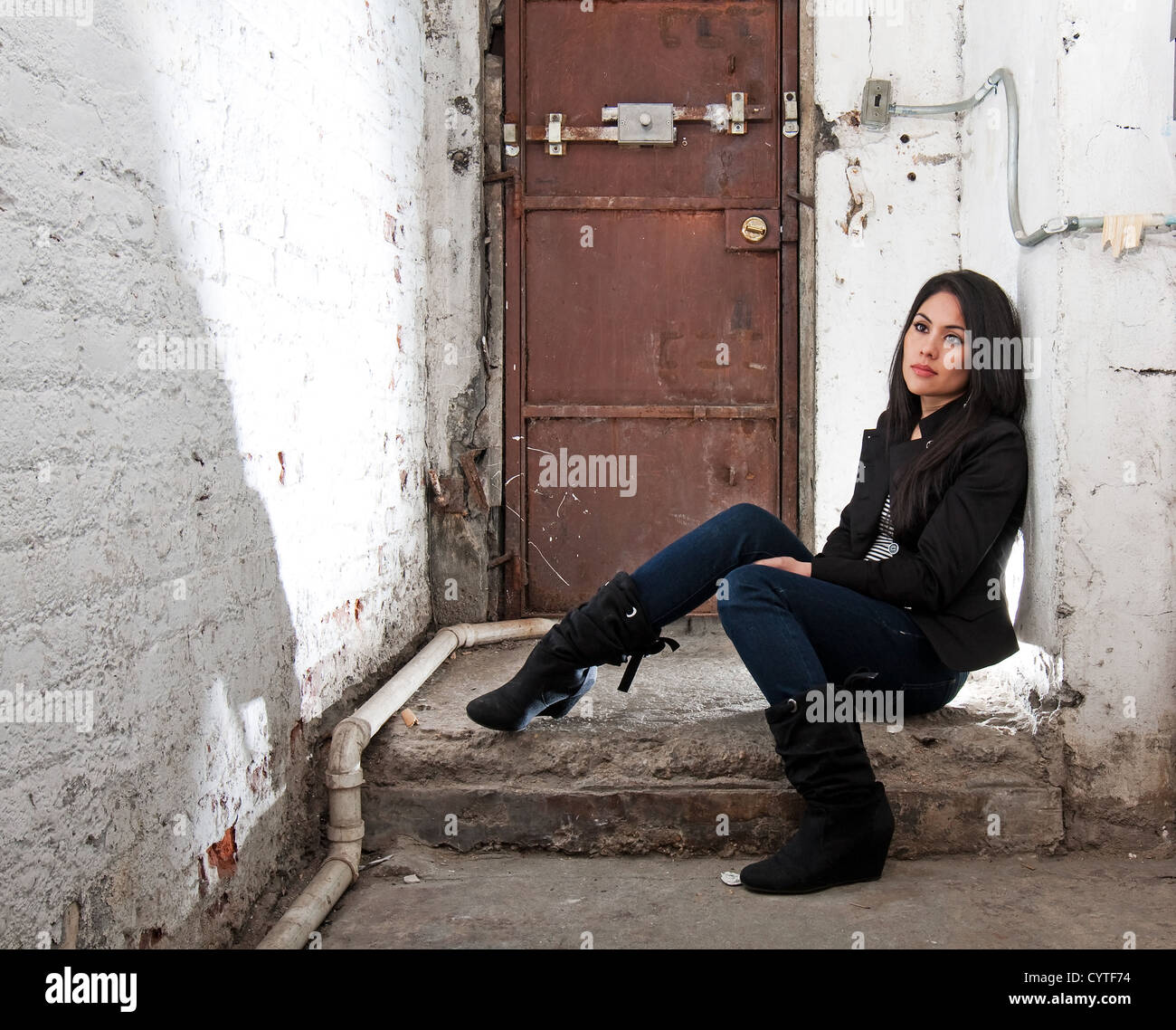 Beautiful Caucasian girl sitting on concrete floor in basement in front ...