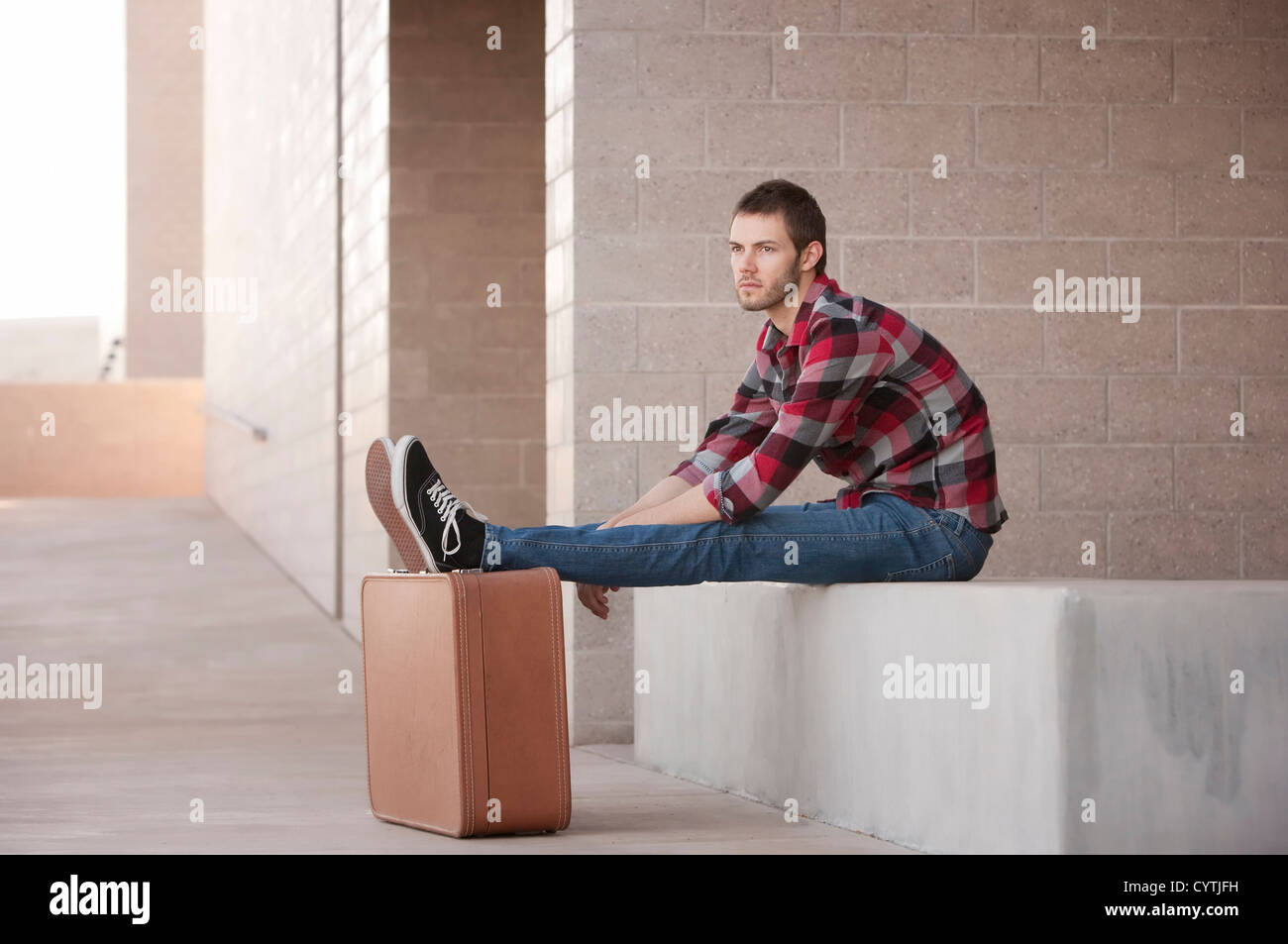 Lanky Young Man Waiting with Feet Propped on Suitcase Stock Photo - Alamy
