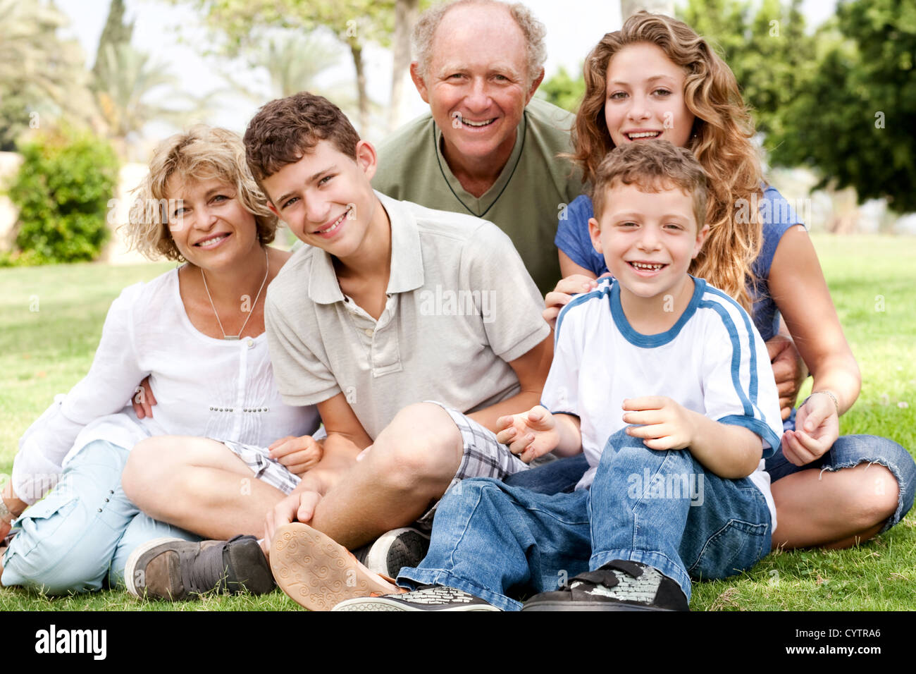 Portrait of happy family of five smiling at camera, relaxing in park ...