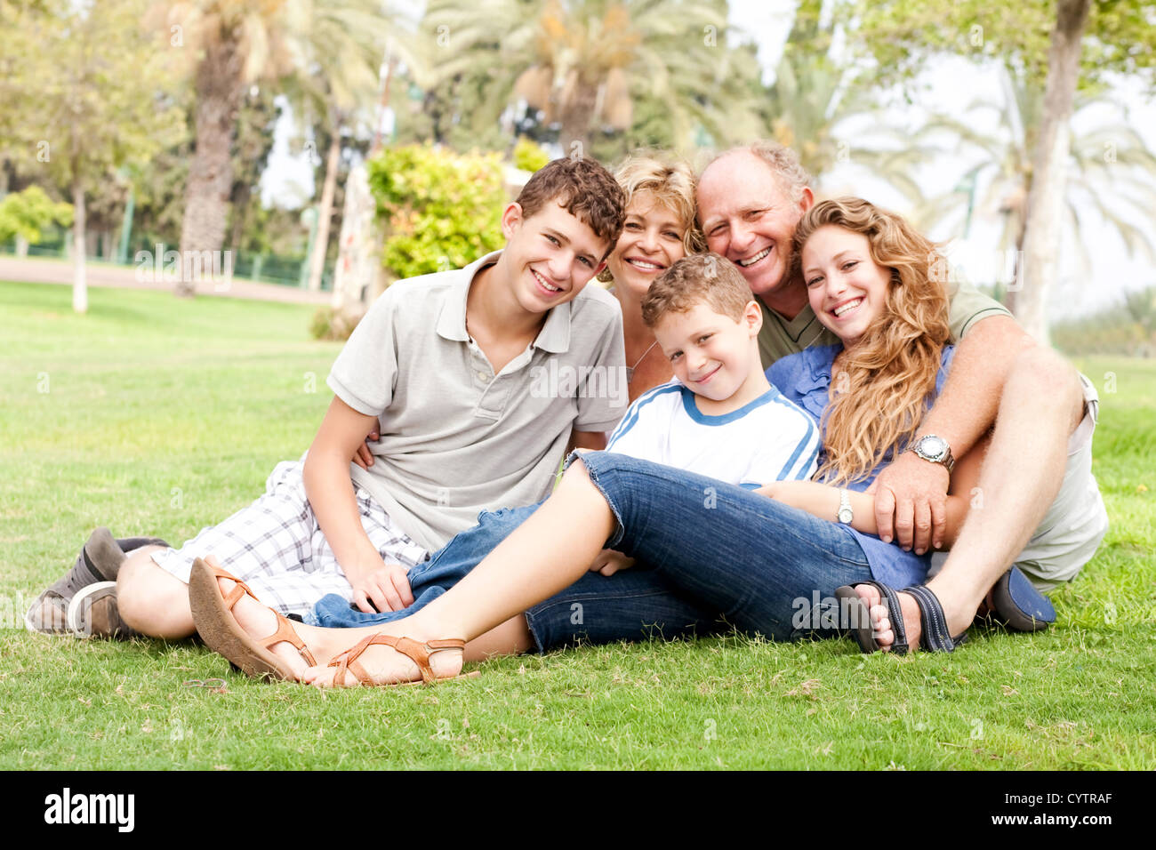 Family of five relaxing on sunny day in the park and smiling at camera ...