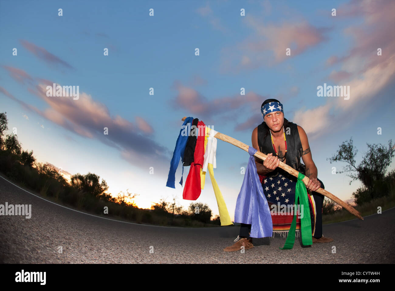 Indigenous man squatting in the middle of a road with ceremonial pole ...