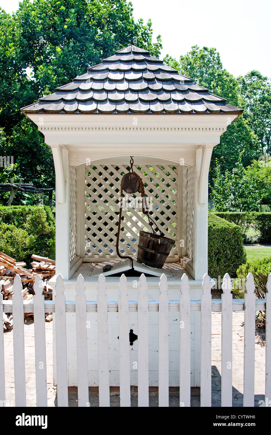 A white wishing water well in Colonial style with wooden bucket on top ...