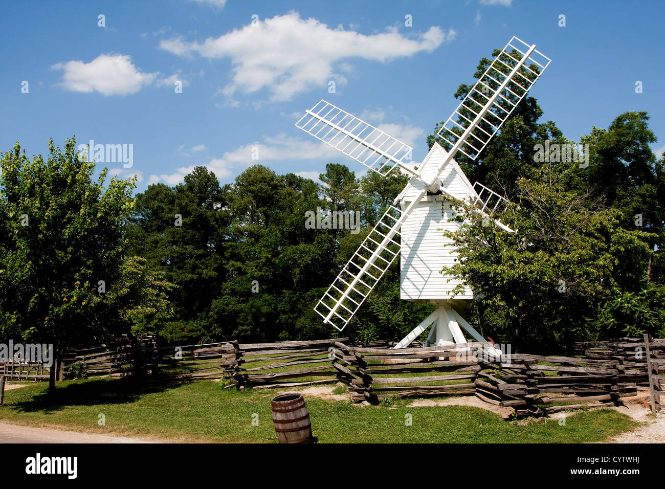 A white wooden windmill in a small meadow behind a wooden fence on a ...
