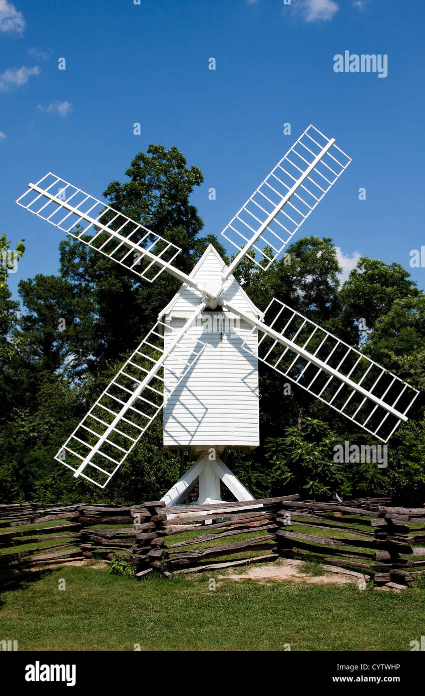 A white wooden windmill in a small meadow behind a wooden fence on a ...