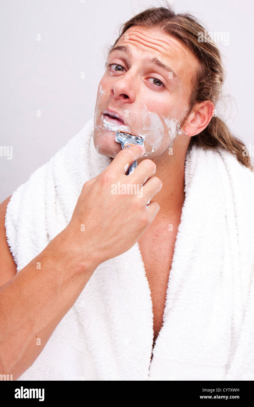 Portrait of a young handsome man shaving as part of his morning routine ...