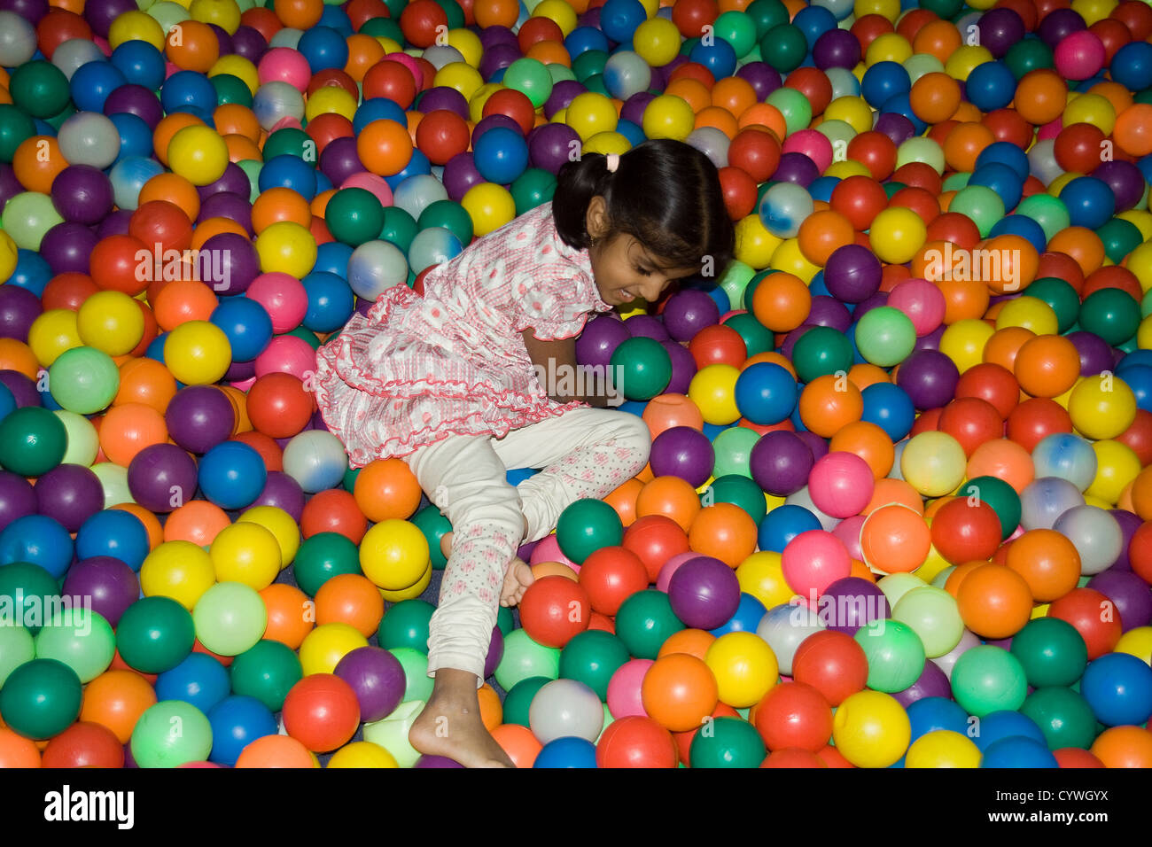 Baby girl caught in between colorful, slippery bed of plastic balls ...