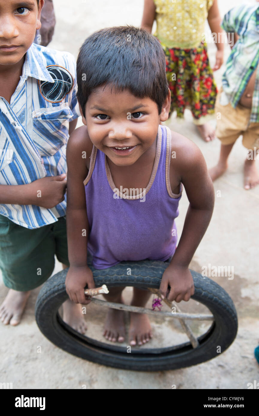 Happy young rural Indian village boy with a tyre looking up to camera ...