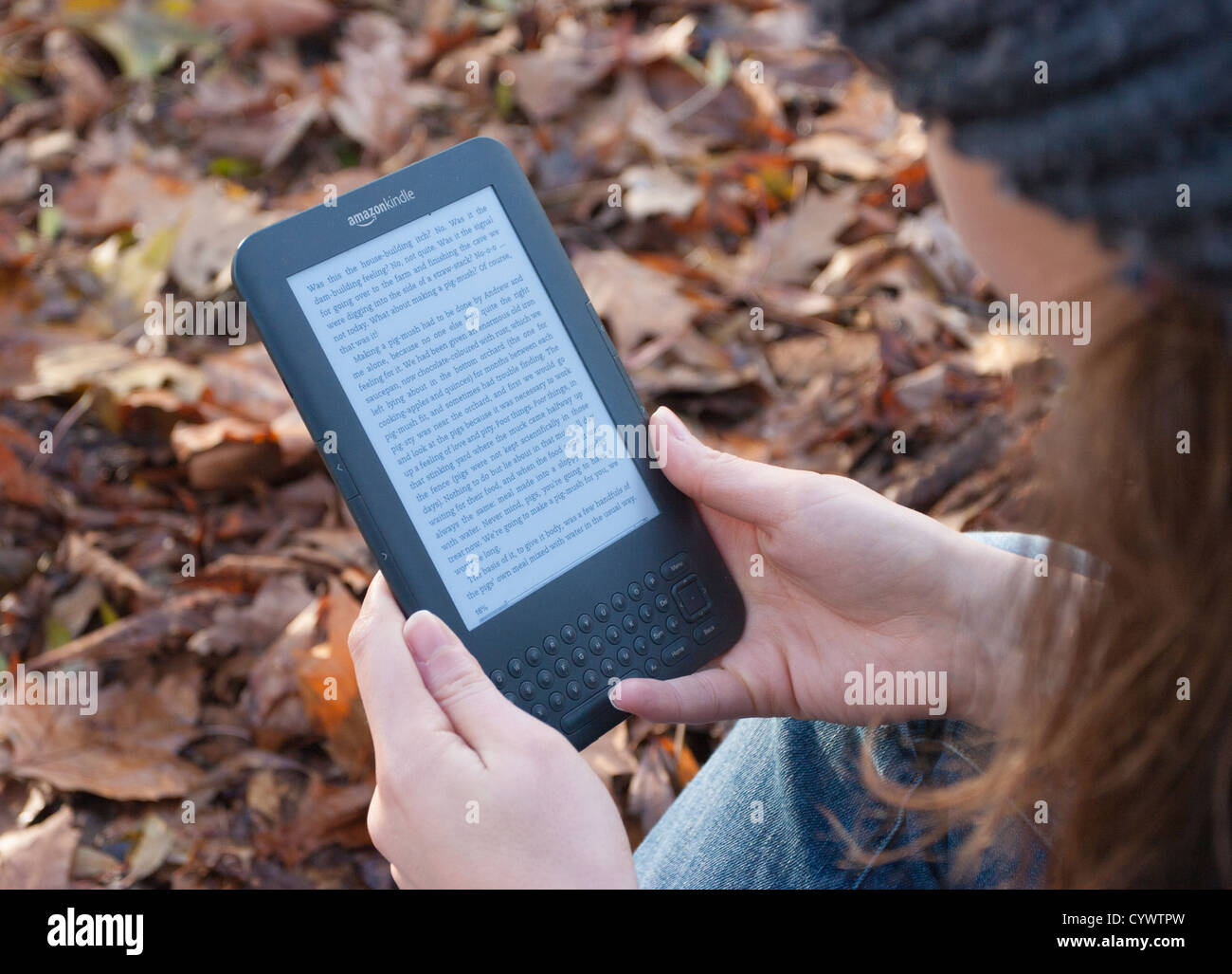 A woman sitting reads an Amazon Kindle ebook reader surrounded by ...