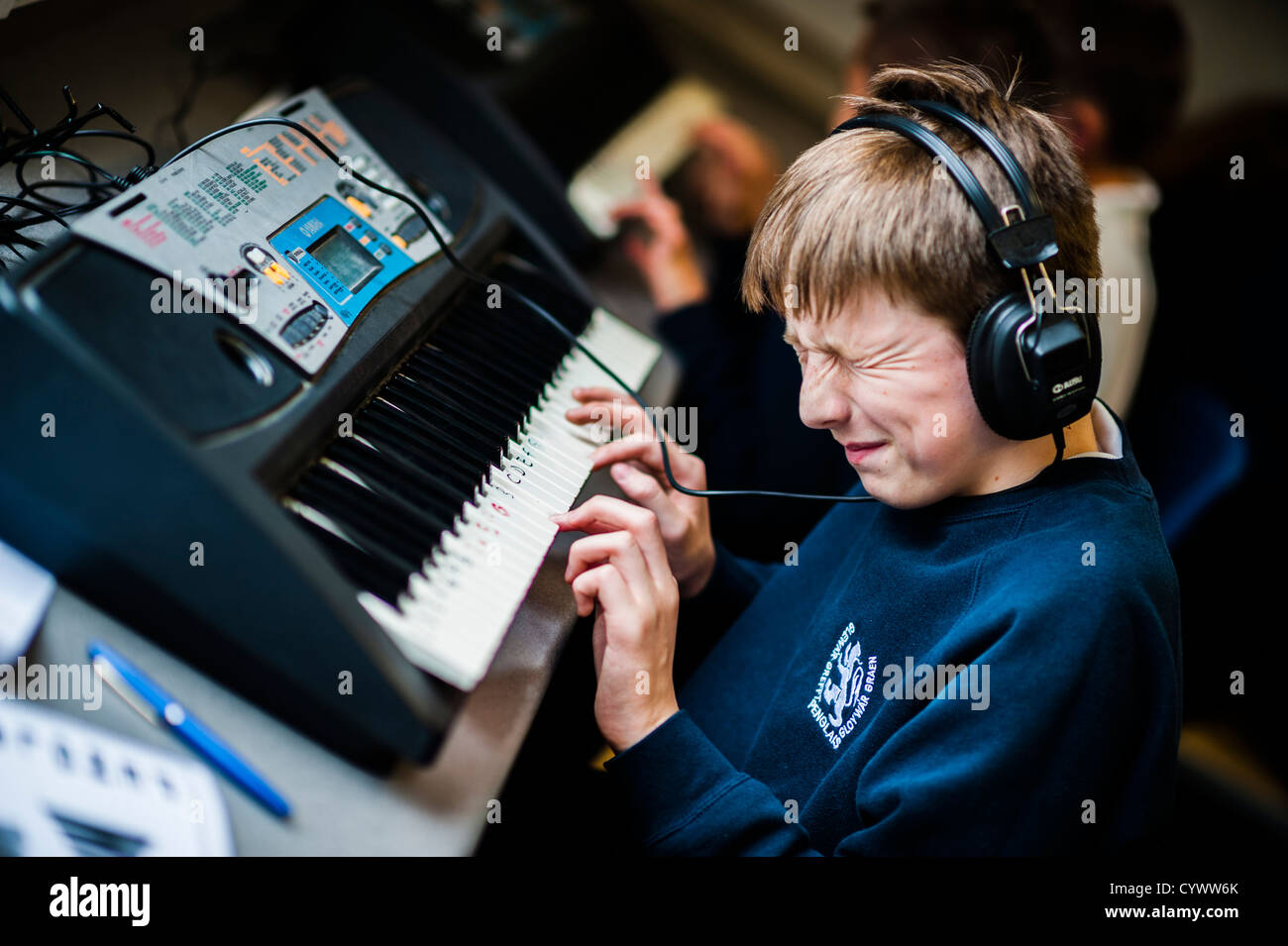 A boy grimacing playing keyboards piano music in a class at a secondary ...