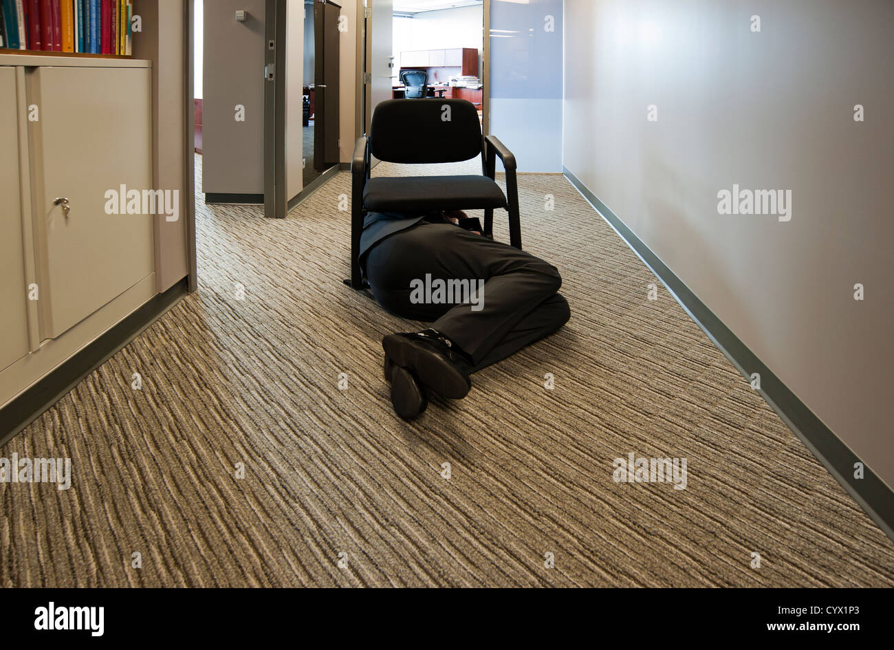 Man laying on the floor under a chair in an office corridor Stock Photo ...