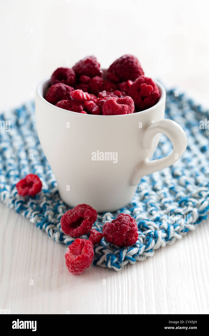Closeup of fresh raspberries in white cup on a blue mat Stock Photo - Alamy