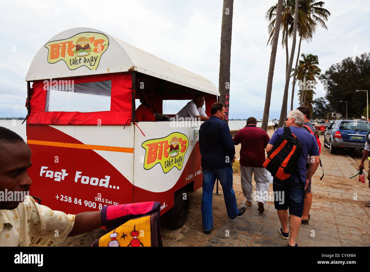 Tourist walk past a food vendor on the foreshore at Maputo harbour ...