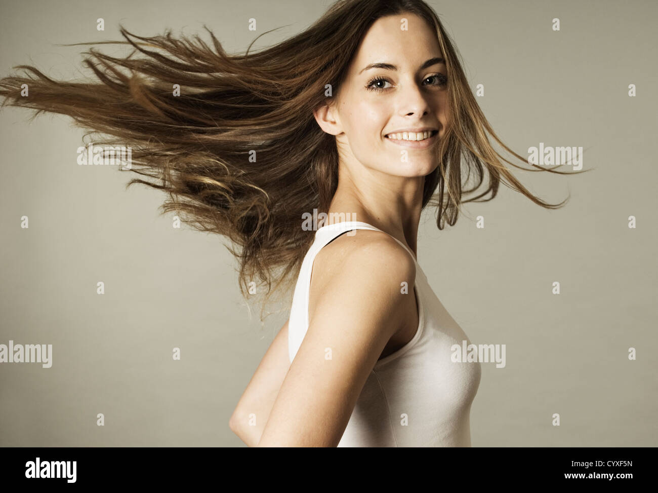 Young woman in sportswear tossing hair against grey background, smiling ...