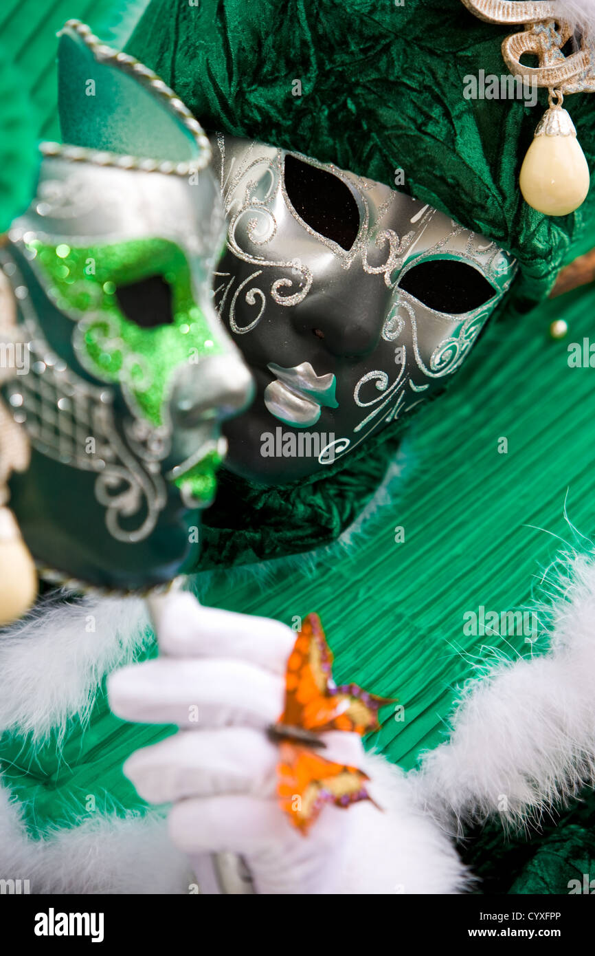 A venetian man in a grey mask and green costume holding a green mask ...