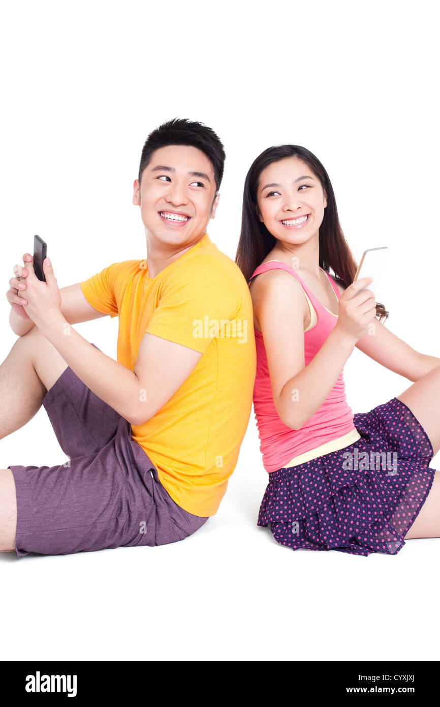 Happy young couple sitting back to back with smart phones Stock Photo ...