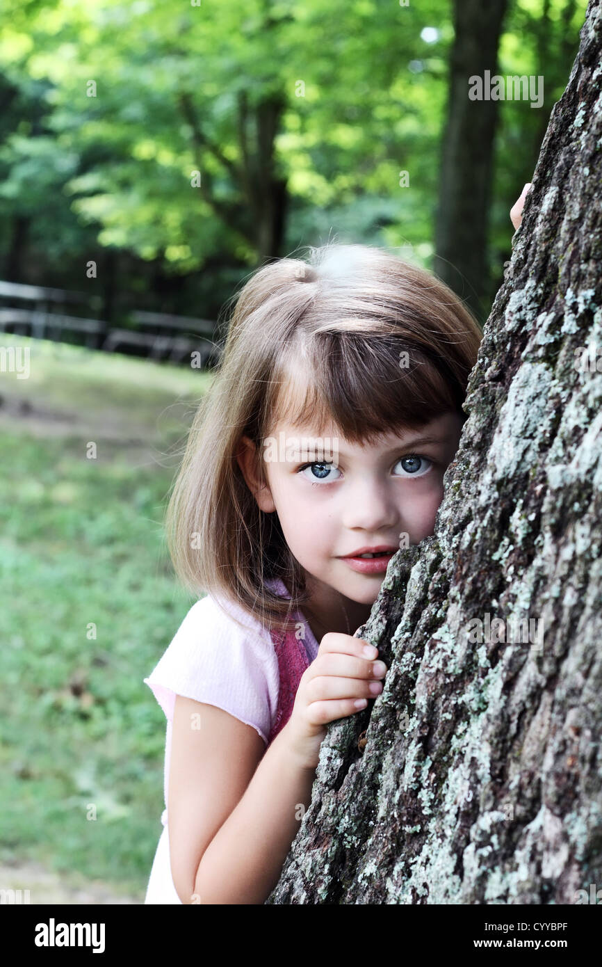 Little girl leaning against a large oak tree and looking at the viewer ...