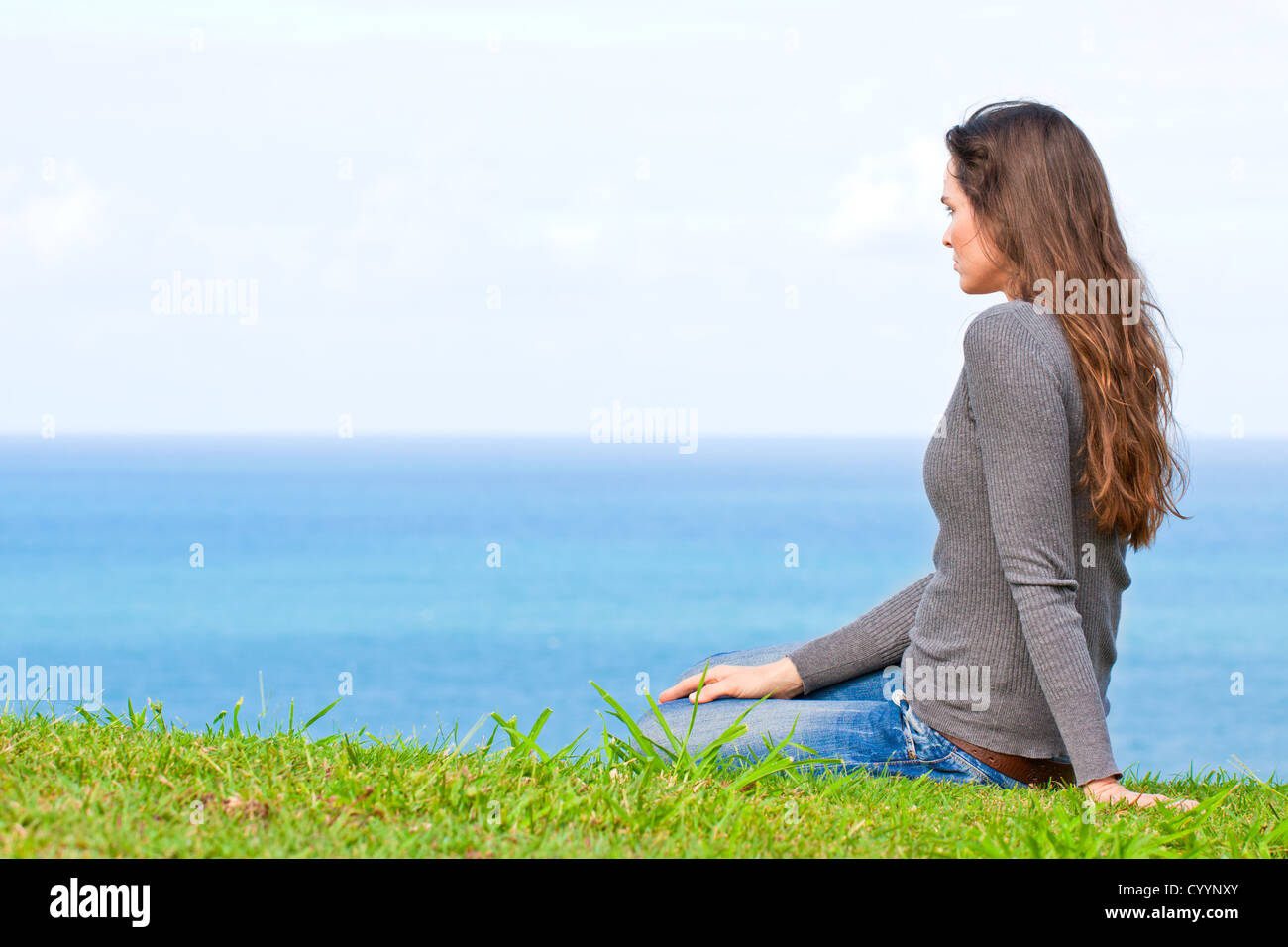 A beautiful sad and unhappy young woman sitting in the green grass ...