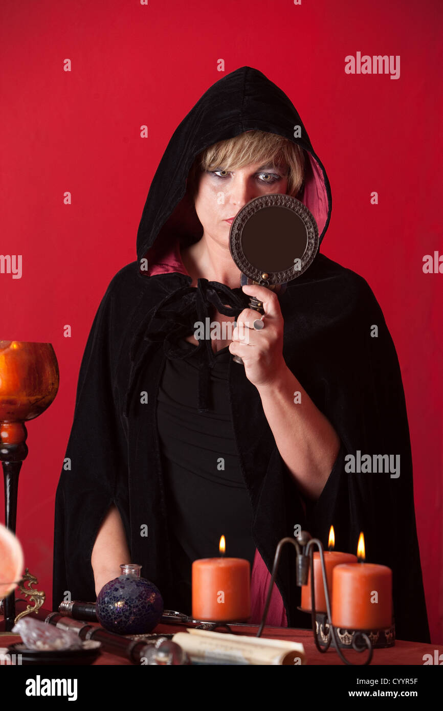 Caucasian witch looks into a mirror over red background Stock Photo - Alamy