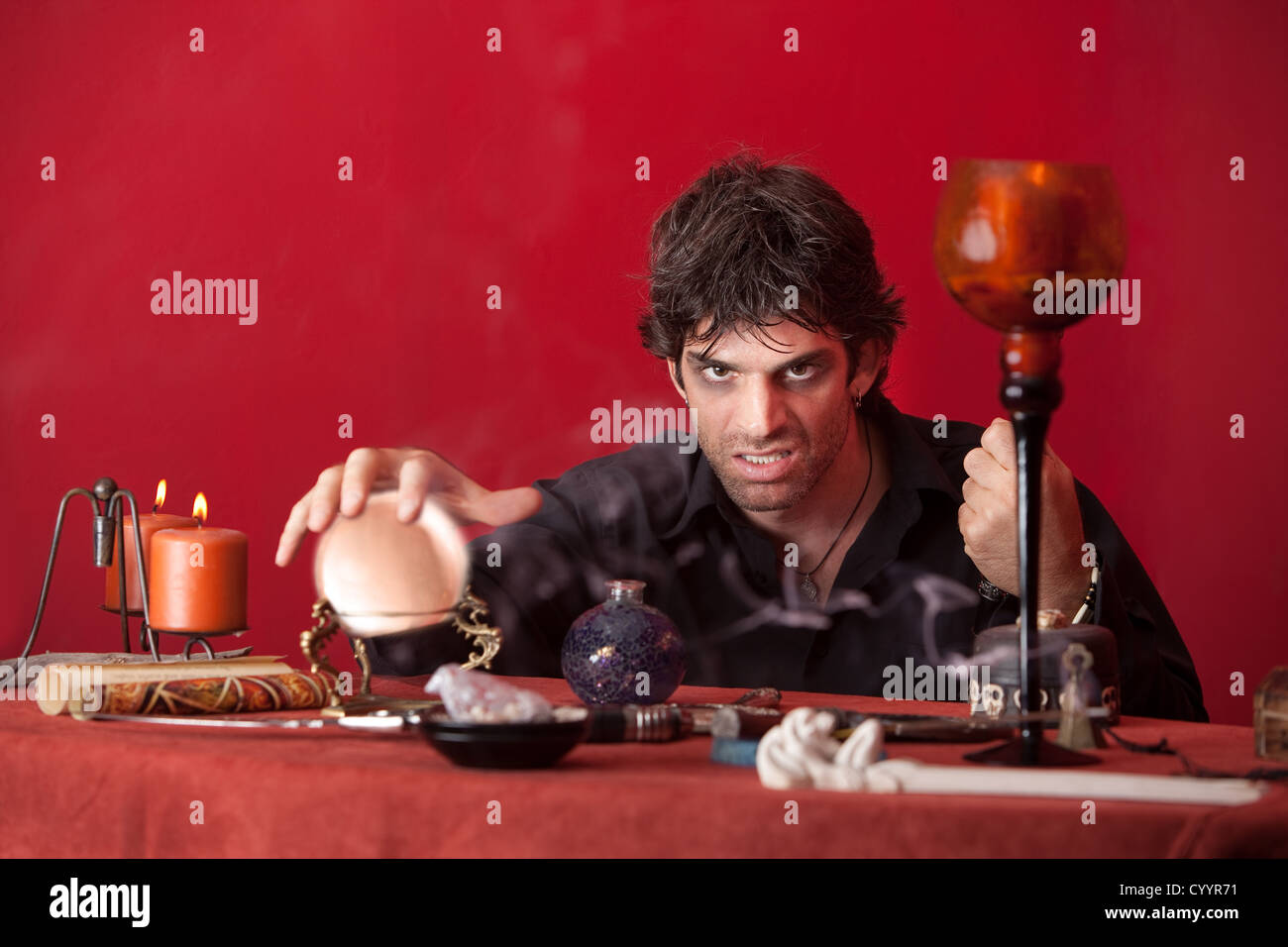 Bad Caucasian wizard with crystal ball over maroon background Stock ...