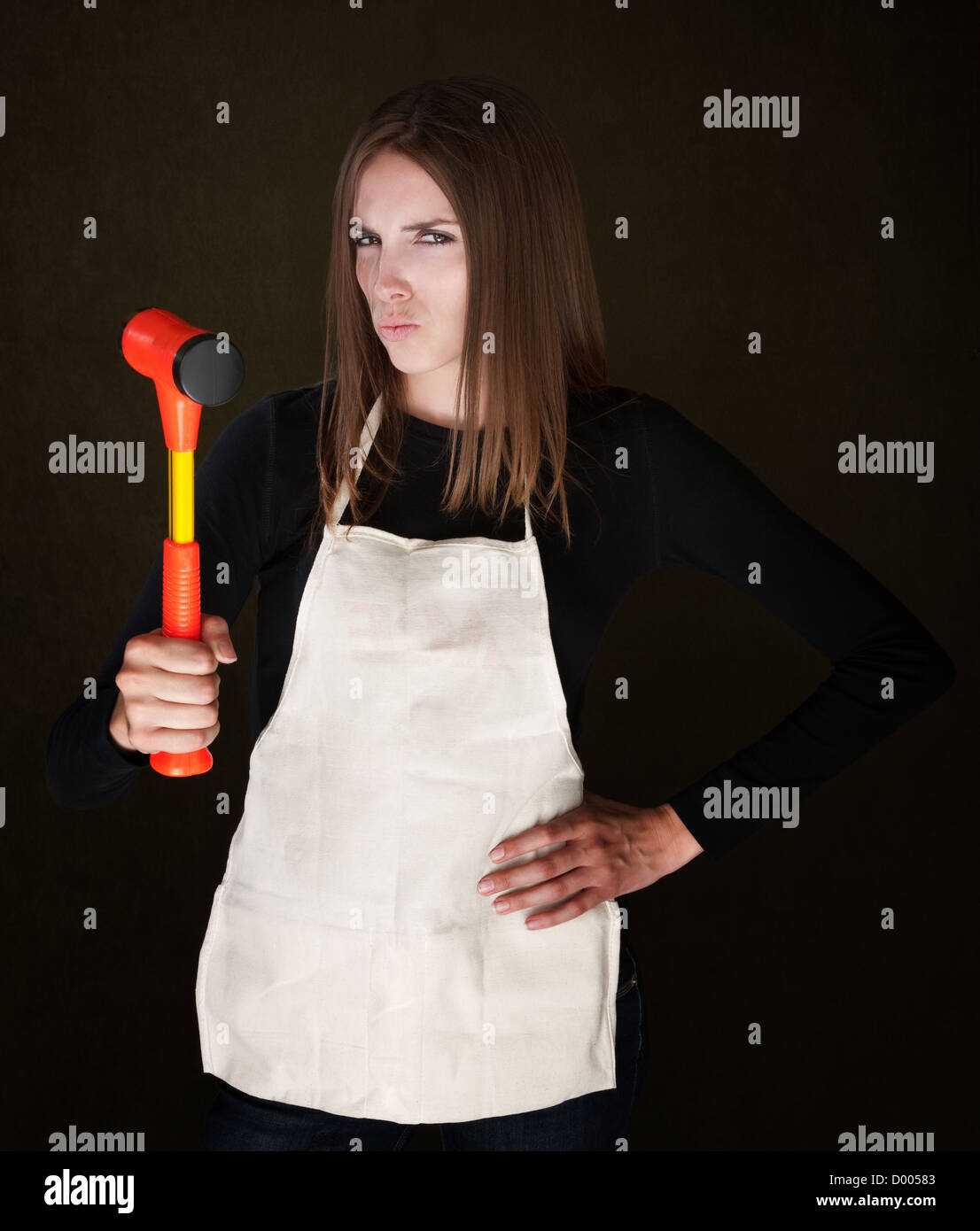 Pretty young woman frowning in smock holding a mallet Stock Photo - Alamy