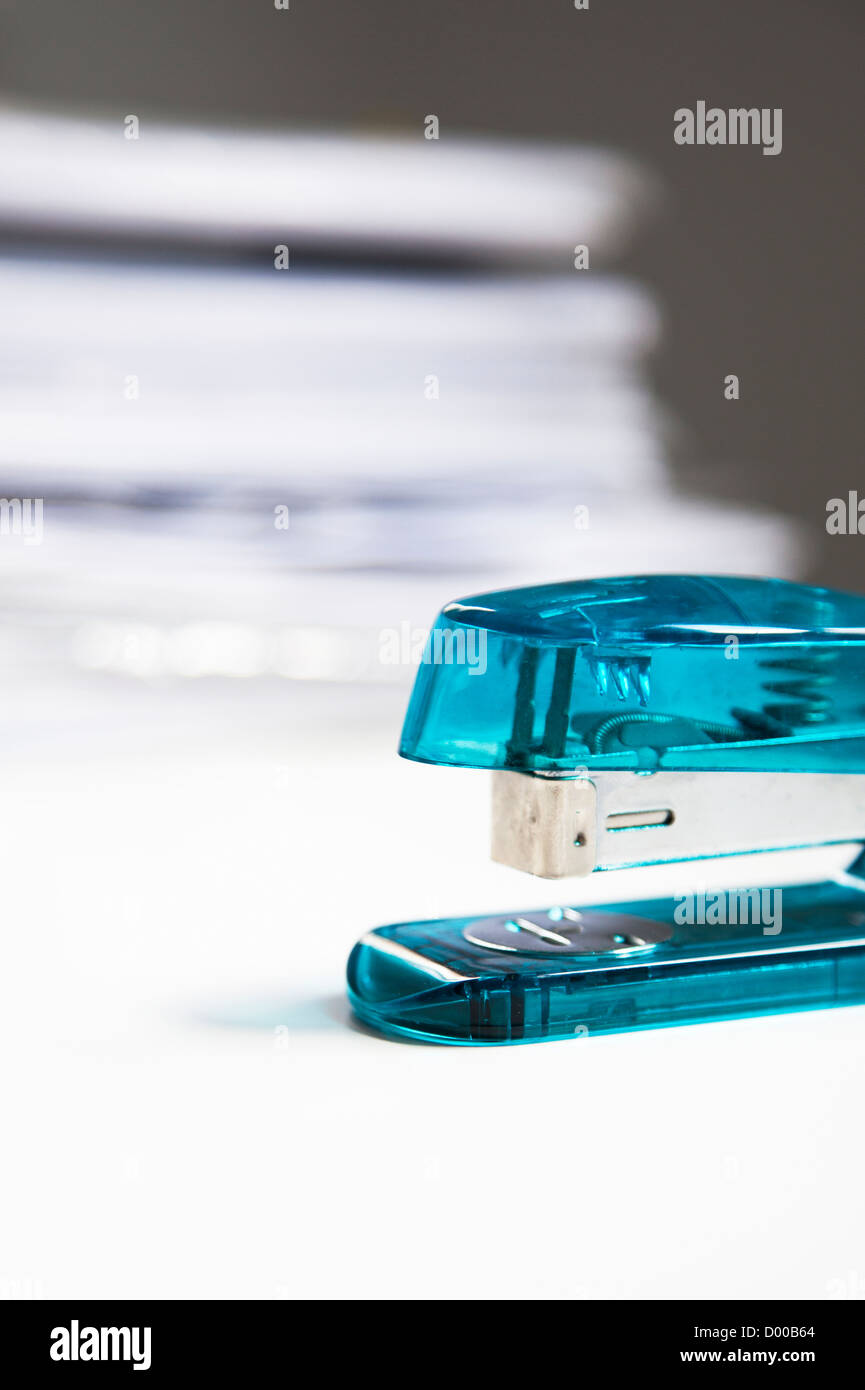 Blue stapler on table with stack of papers in background Stock Photo ...