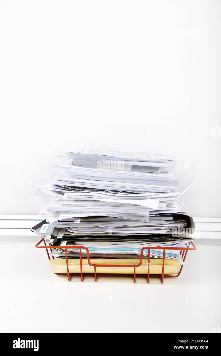 Documents overflowing in desk tray against white wall Stock Photo - Alamy