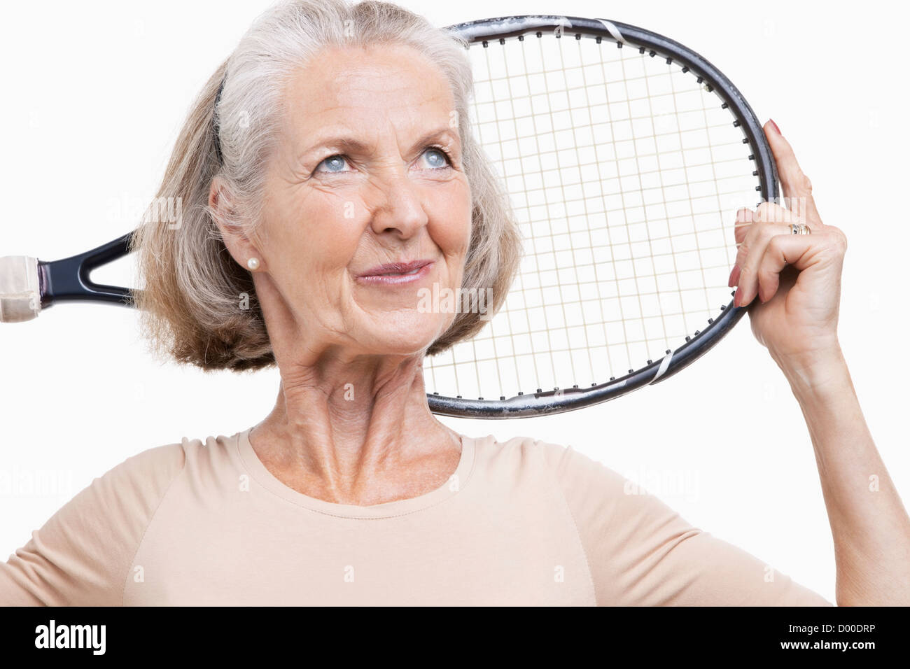 Senior woman holding tennis racket over her shoulder against white ...
