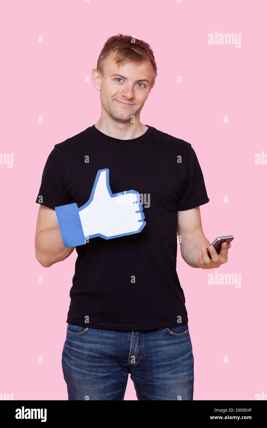 Portrait of a happy young man with cell phone holding fake like button ...