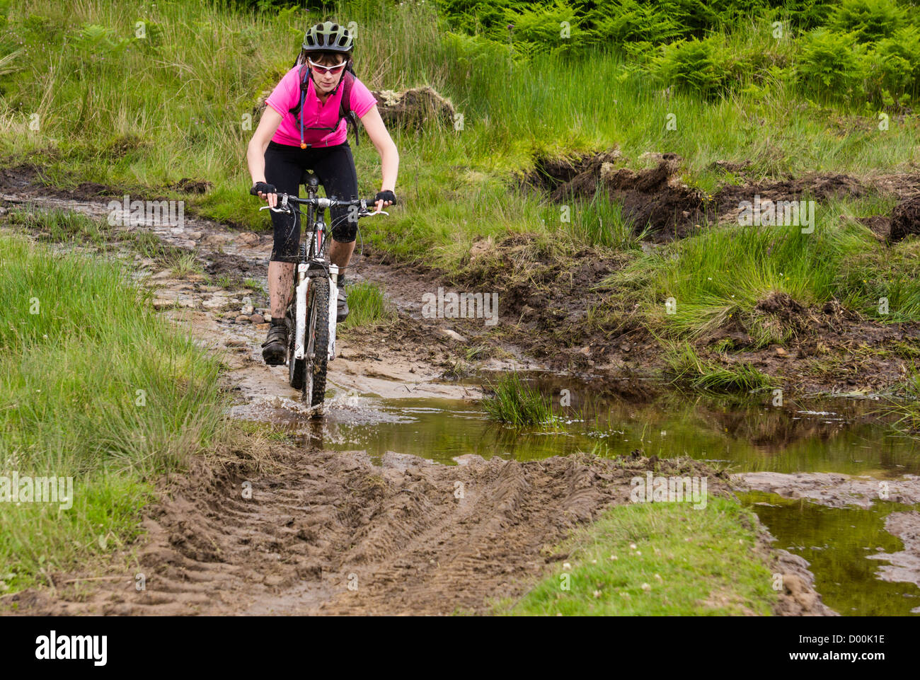 A woman riding her mountain bike through a muddy puddle on a dirt track ...