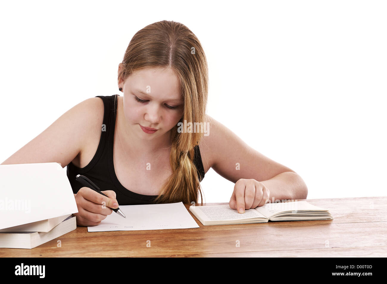 Beautiful young girl sitting by table and writing on white background ...