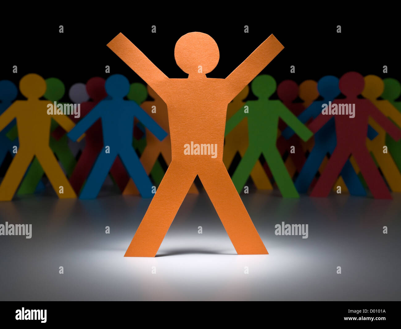 A orange paper figure stands under the spotlight in front of multicolor ...