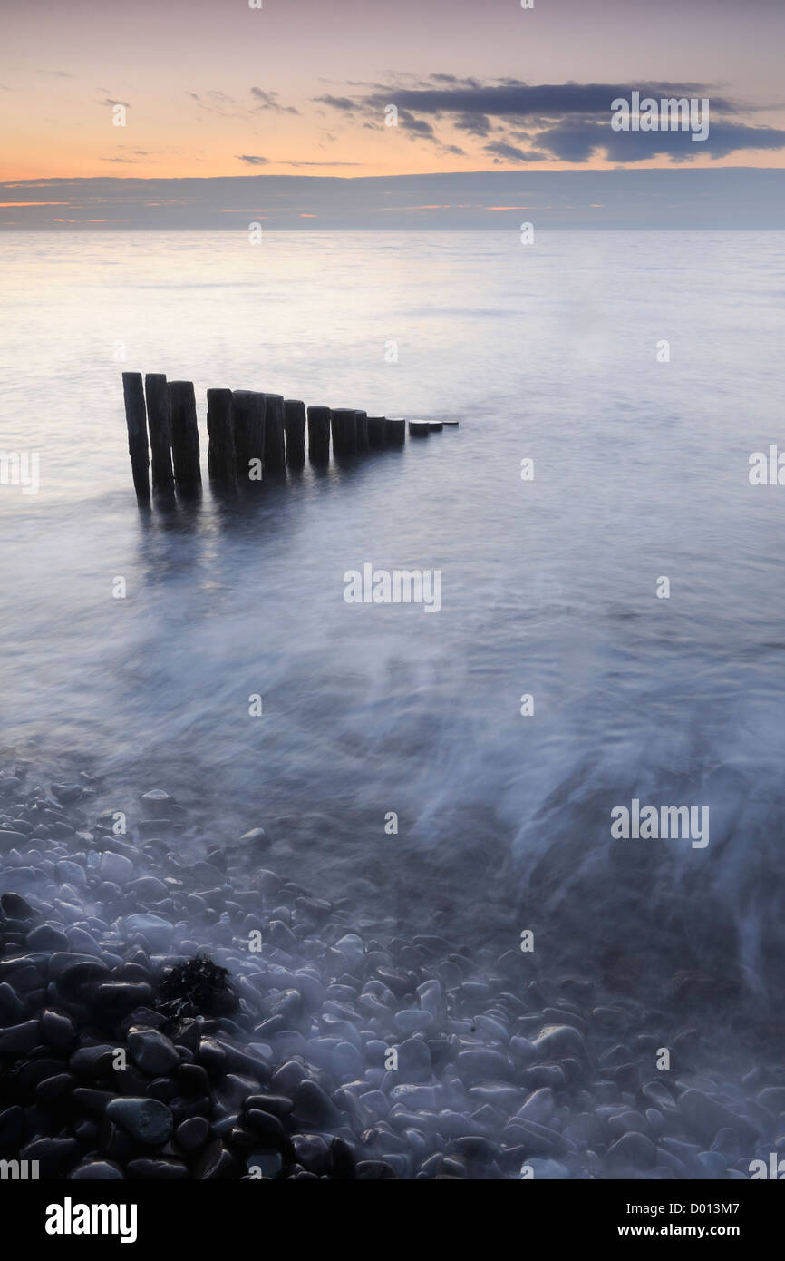 Incoming tide washing over rocks and wooden groynes on Bossington Beach ...