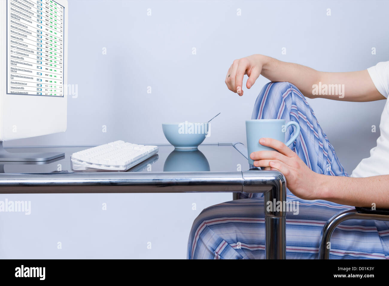 Young man in pyjamas sitting at computer desk holding cup Stock Photo ...