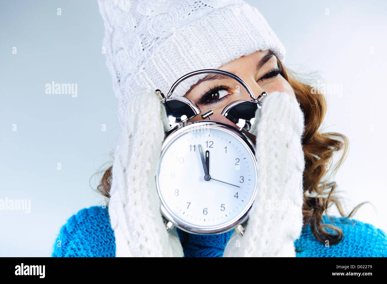 Beautiful young girl in winter clothes peeping through alarm clock ...