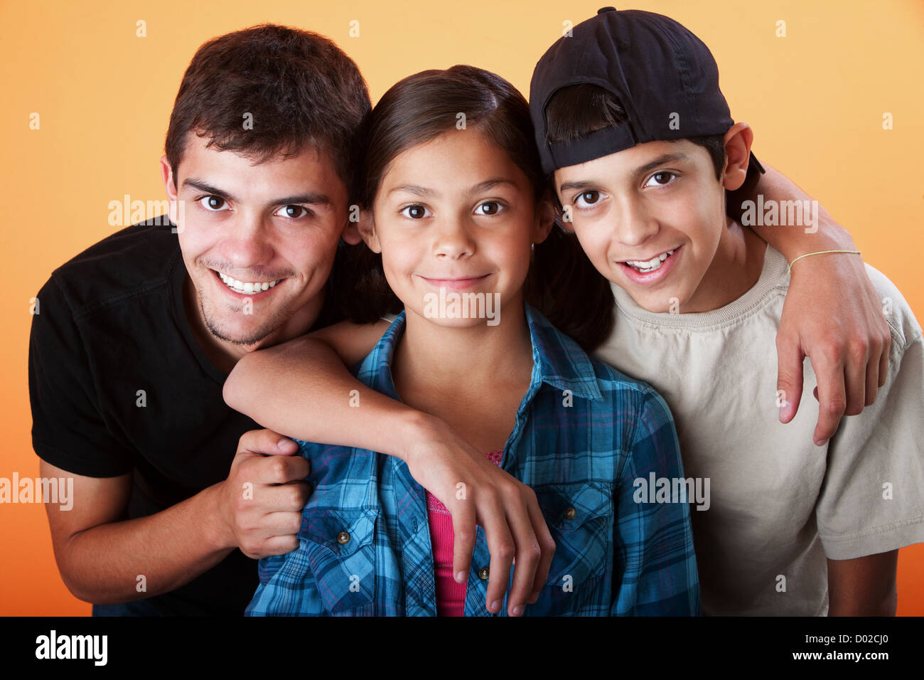 Caring brothers with their sister smiling on orange background Stock ...