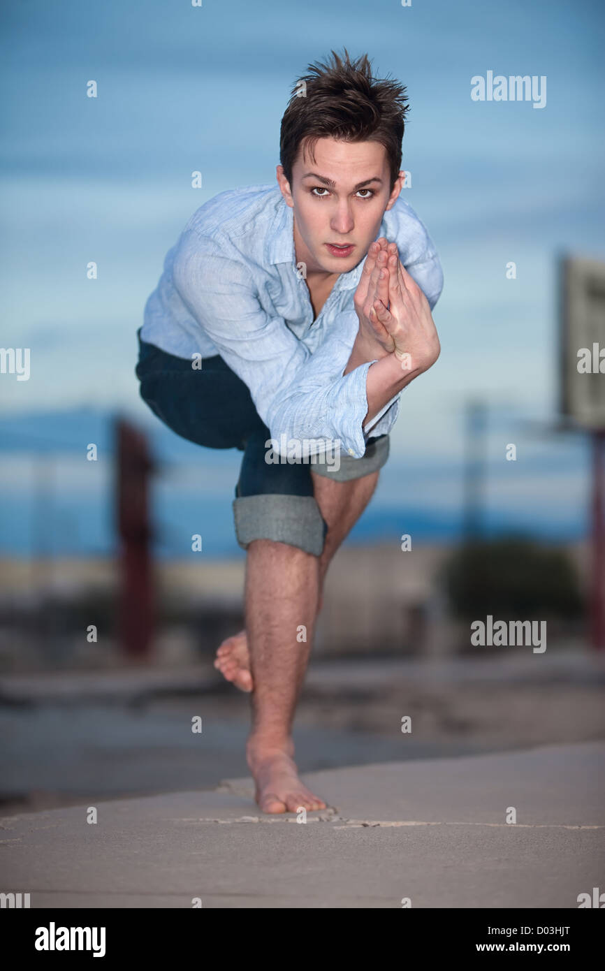 Young Caucasian man crouches on one leg for yoga exercises outdoors ...