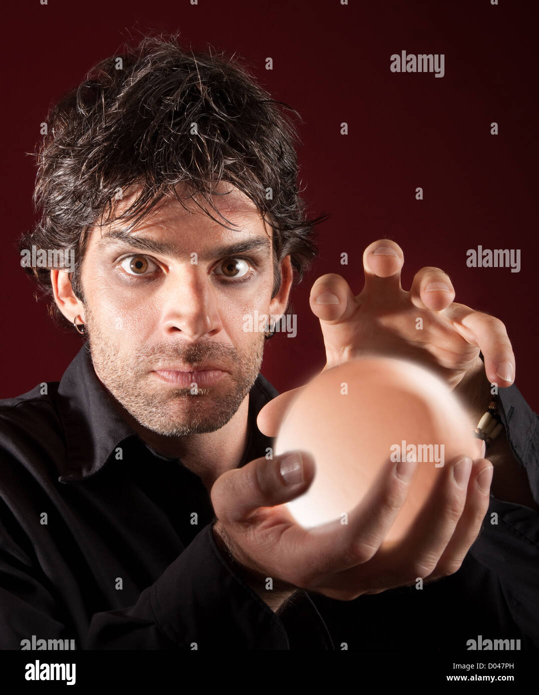 Serious fortune teller holds crystal ball over maroon background Stock ...