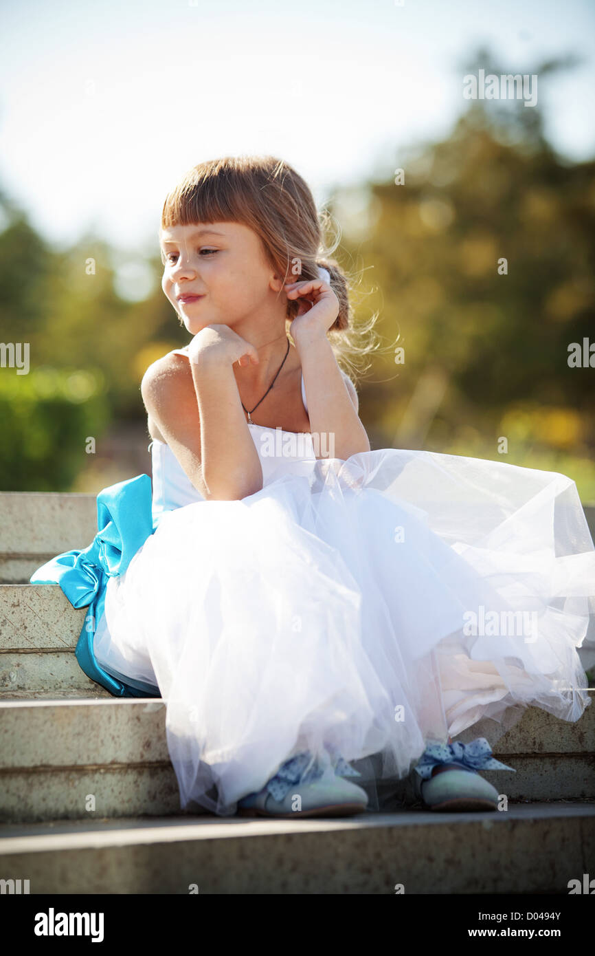 Lovely little bridesmaid sitting outdoors at wedding Stock Photo - Alamy