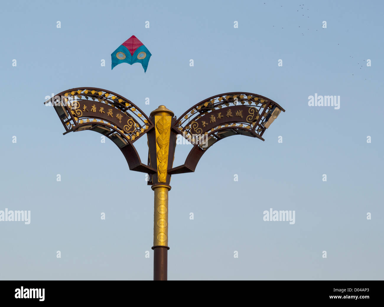 Chinese lamp post with kite flying above in blue sky and birds in ...