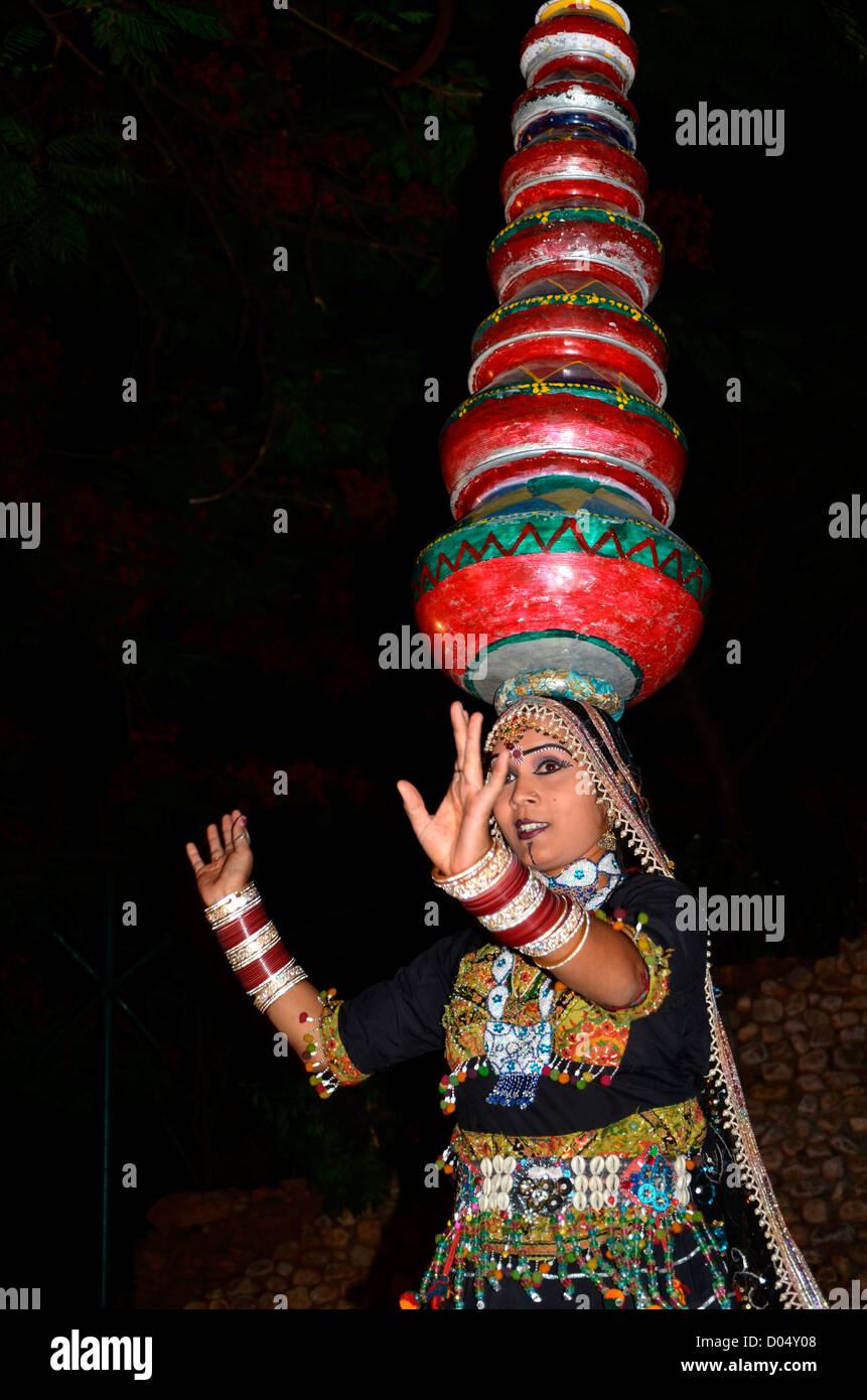 A female folk dancer dancing with a set of colored pitchers on head ...