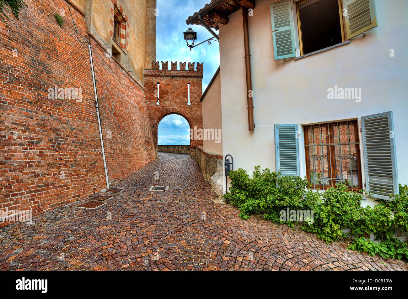 Narrow cobbled street among house and brick wall of medieval castle in ...