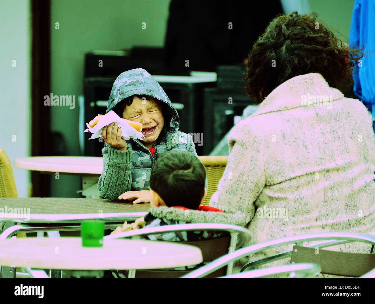 child crying at an outdoor cafe whilst holding a hot-dog Stock Photo ...