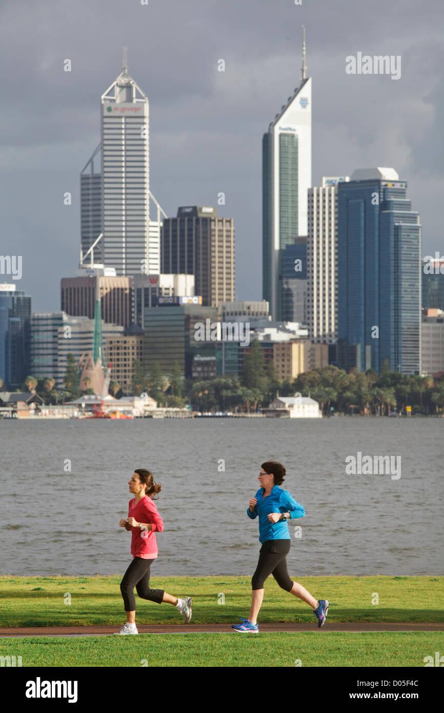 Two women jogging on path beside river with city in the background ...