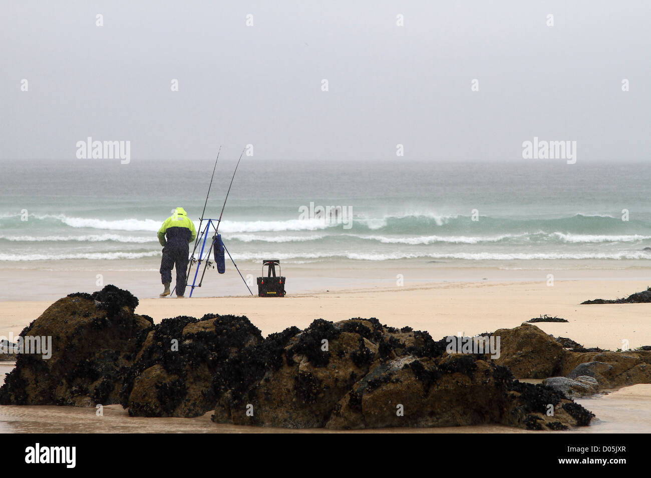 Man fishing in heavy rain in the sea, on the beach at St Ives, Cornwall ...