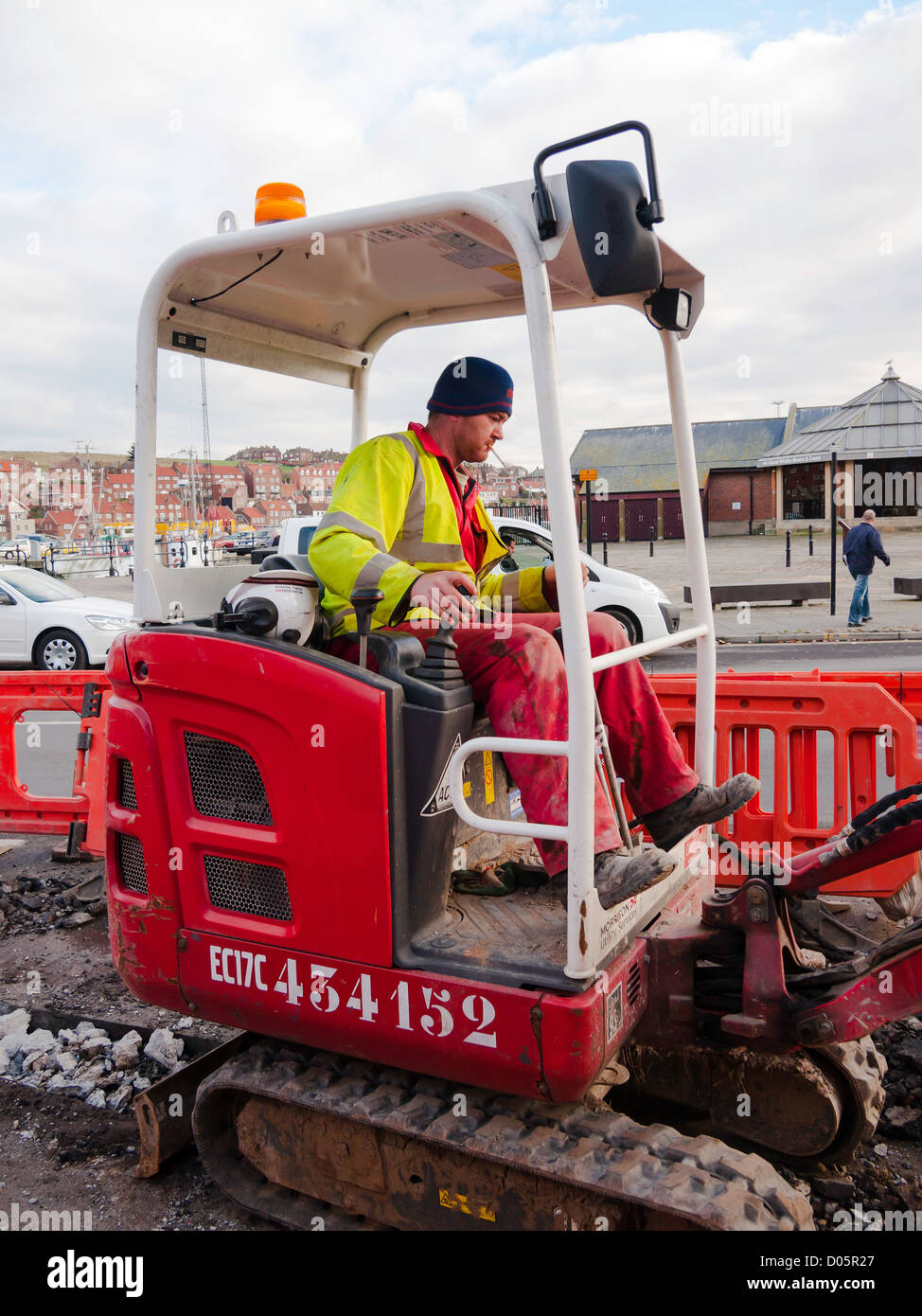 Workman operating a small Bobcat excavator digging a trench in the ...