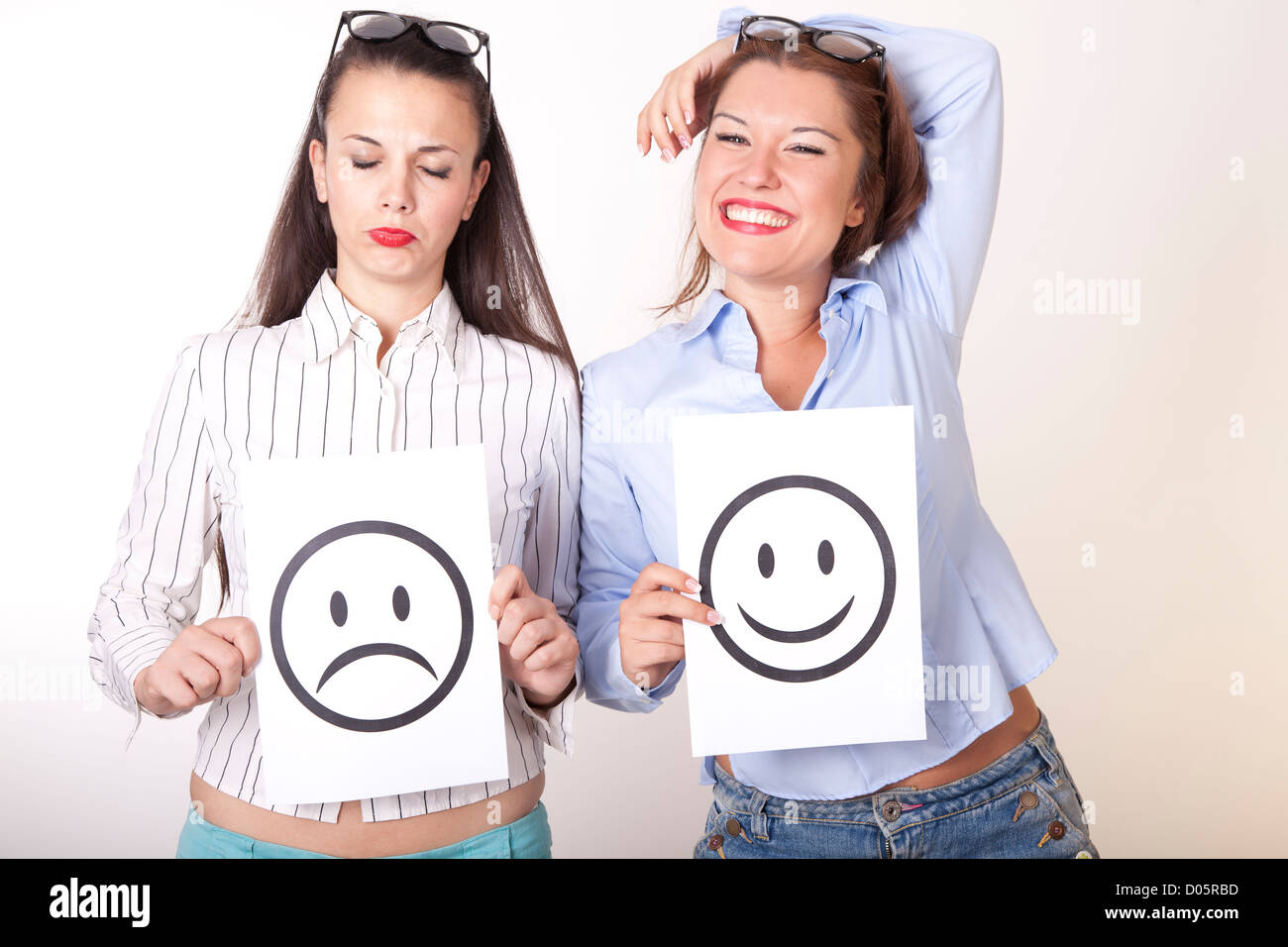 Portrait of a two young beautiful women holding smiley and sad smiley ...