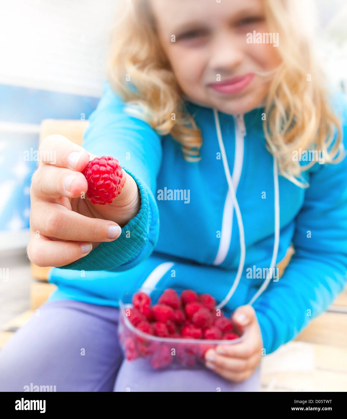 Little blond active girl held out fresh raspberry from his full box ...