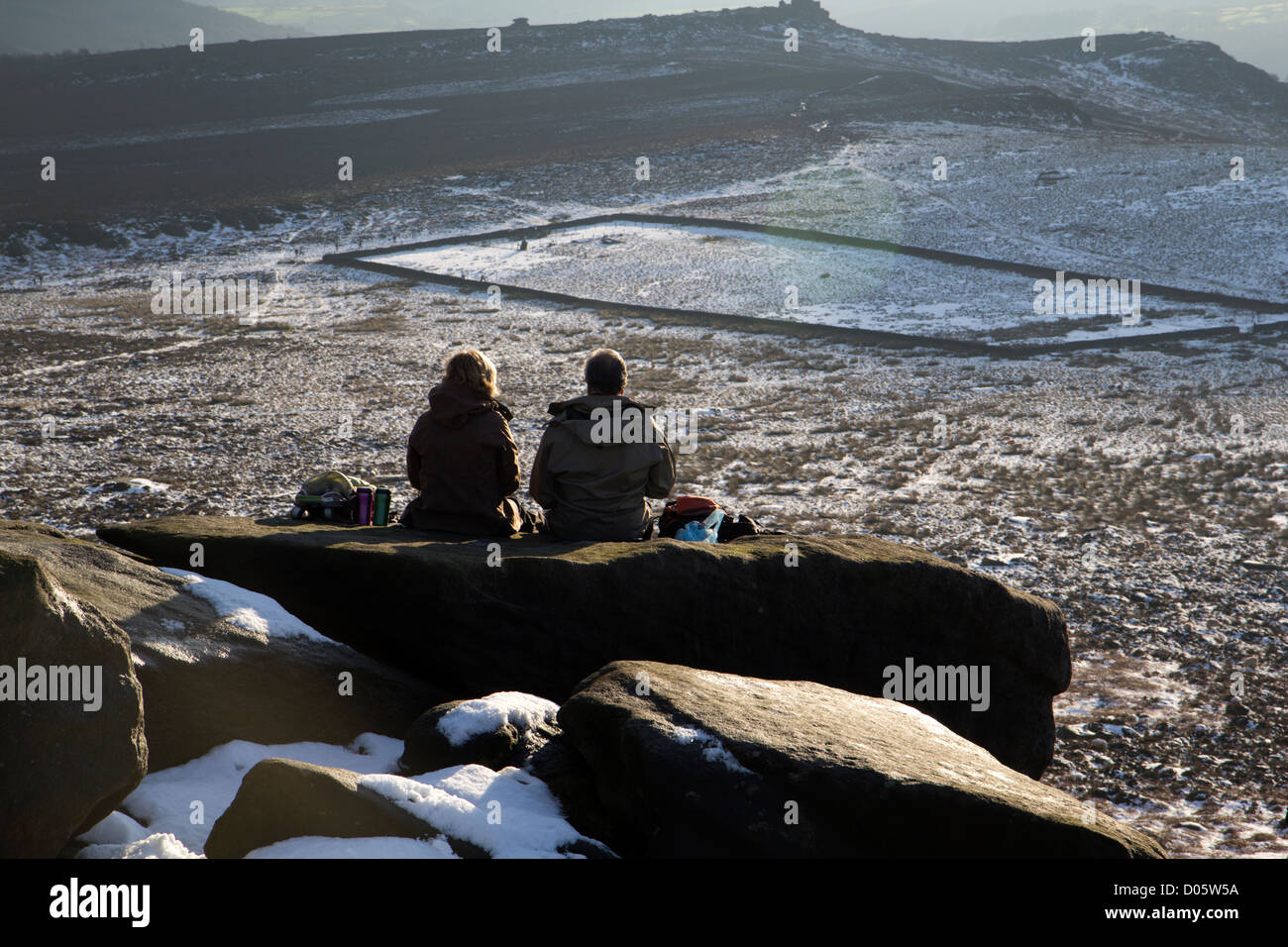 Couple sat on rocks looking out at the snow covered Peak District ...