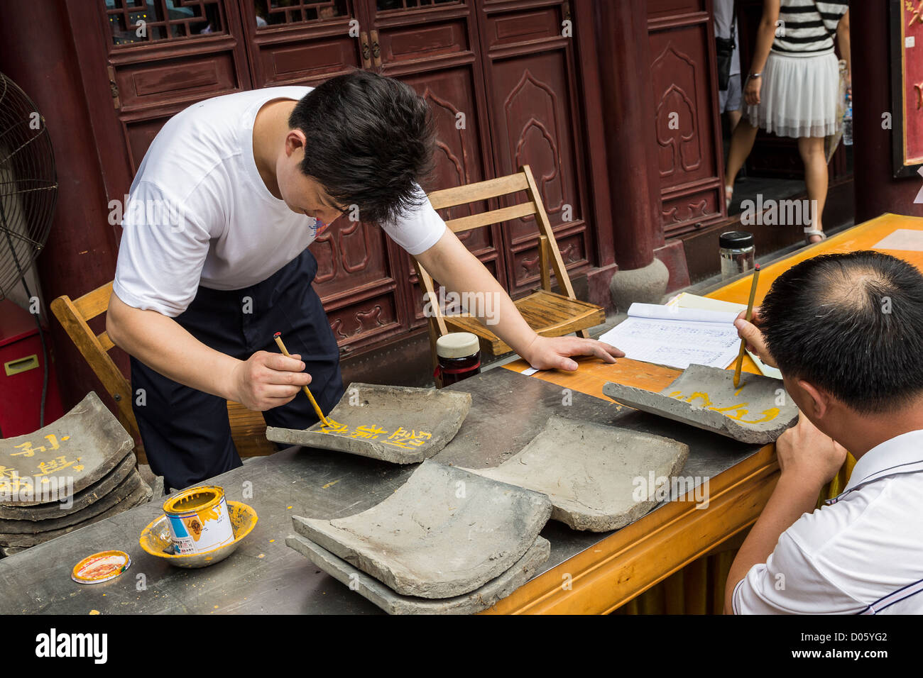 A man writes a prayer on a temple tile at Chenghuang Miao or City God ...