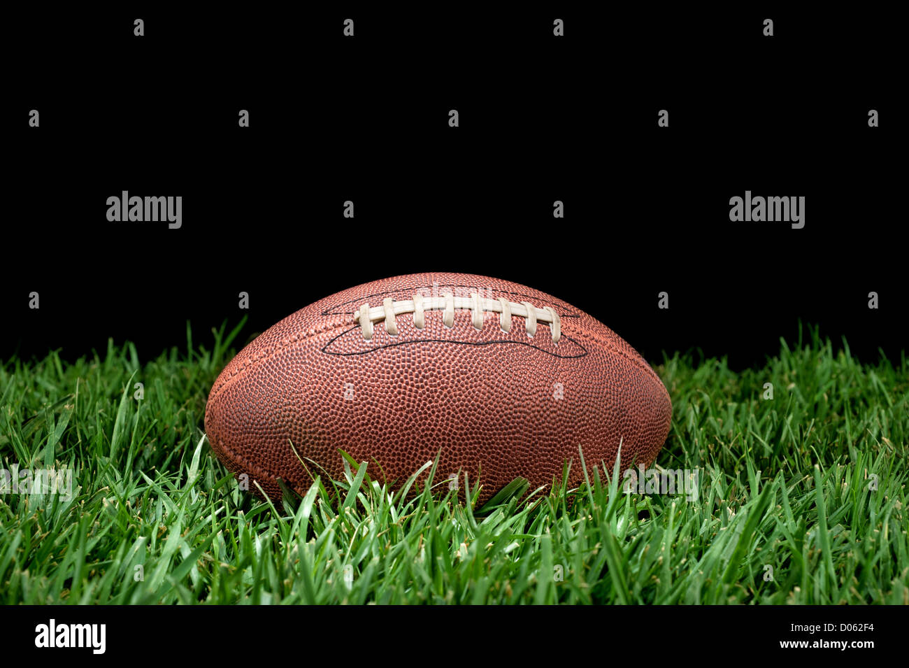 A pigskin football lying in the grass against a black background for ...